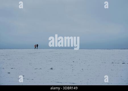 People walk across the snow-covered frozen lake Elbsee under a clear ...