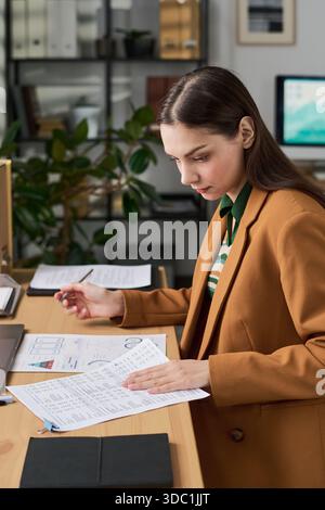Young businesswoman reviewing financial documents and writing notes at ...
