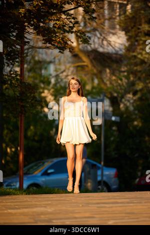 A girl in a light summer dress holds a branch with green leaves, a ...