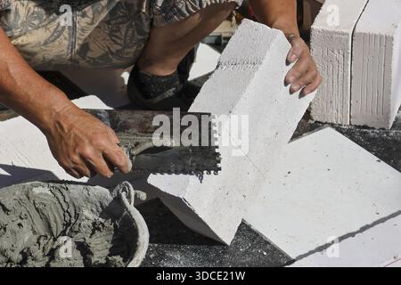 A closeup of a person applying cement on a brick with a spatula in a ...