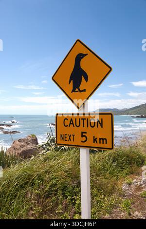 Coastal road with penguin warning sign offers a view of the blue sea ...