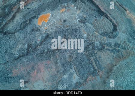 Dark grey mining sludge surface with bright orange toxic liquid puddle ...