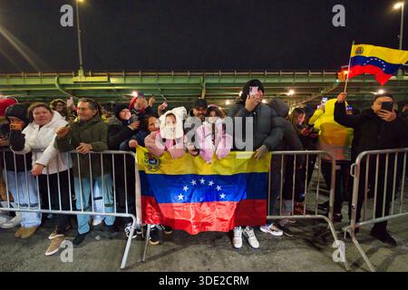 People stand behind a metal barrier, holding Israeli and American flags ...