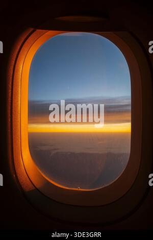 A commercial airplane flying through an orange sky during sunset ...