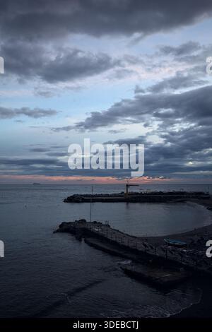 Sea stretching to the horizon with breakwaters on a cloudy nightfall ...