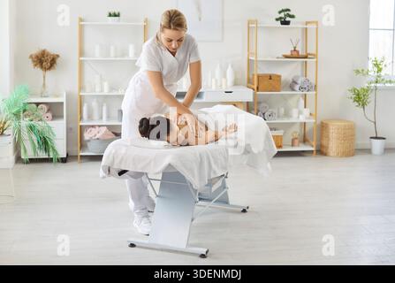 Professional masseuse performing back massage to Caucasian male client ...