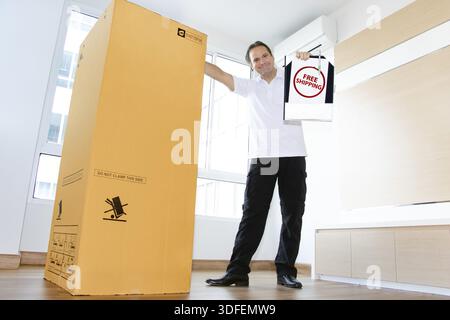 A man shows a large package in an empty room. The postman delivers the ...