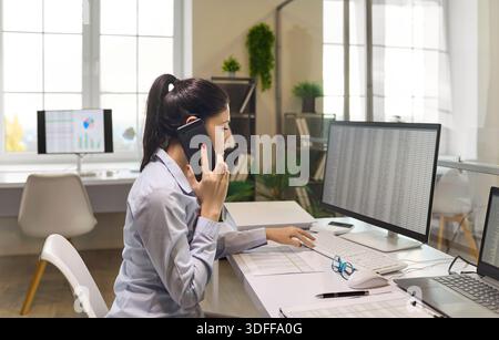 Financial advisor on phone at desk, analyzing spreadsheets on computer ...