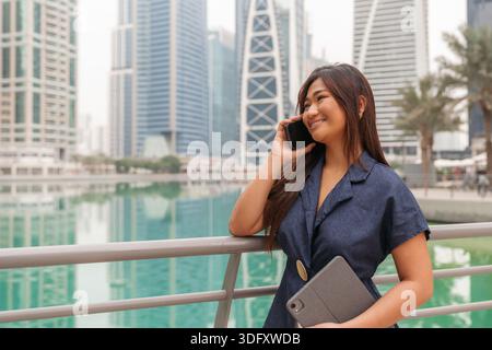 A woman works on her smart phone as she sits on a bench on a sidewalk ...