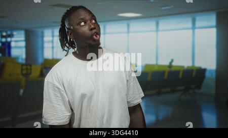 Man with pucker mouth looking up in airport terminal wearing white ...