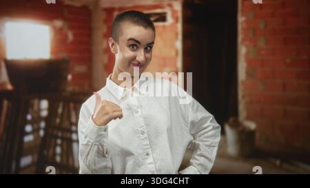 Woman with short buzzcut pointing thumb over shoulder and wearing white ...