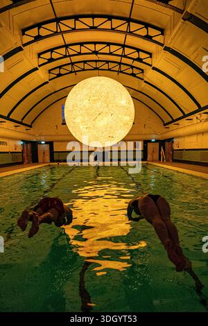 People dive into the water beneath Helios, an illuminated sun ...