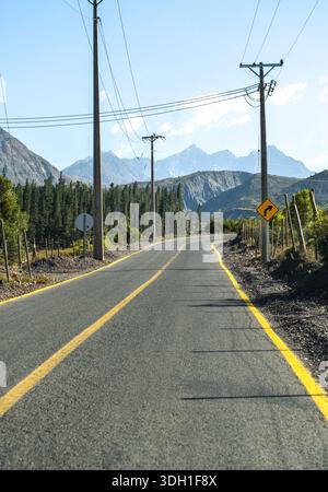 A paved road curves through a landscape of grass and trees under a ...