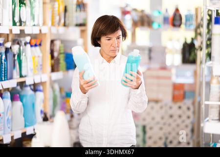 Female buyer chooses shampoo or shower gel in household goods ...
