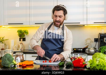 Middle-aged man happily chopping red pepper for fresh salad while ...