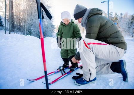Father helping son with skis in Finnish forest. Active family winter ...