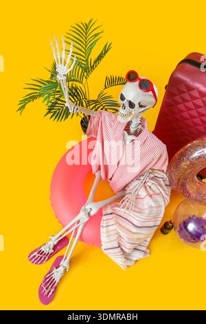 Human skeleton, beach accessories and suitcase on yellow background ...