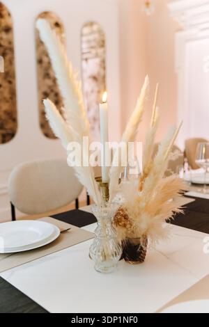 Dining table, vase of pampas grass and wine bottle in room Stock Photo ...