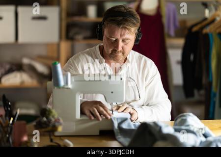 Man seamstress operating by sewing machine, manufactures clothing ...