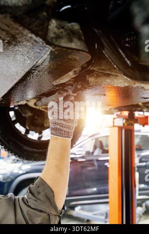 Mechanic working under lifted car in workshop. Specialist is examining ...