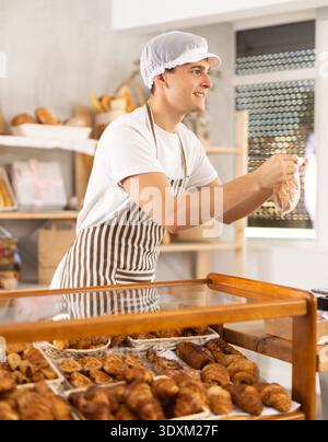 Smiling young bakery seller offering freshly baked pastries Stock Photo ...