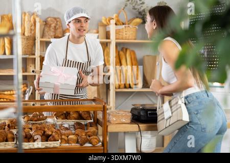 Young bakery seller offering gift-wrapped box with baked treats to ...