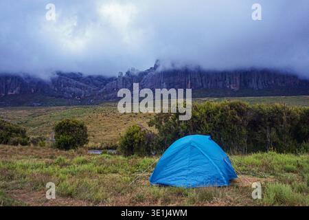 Camping tent stands on a grassy bank next to a flowing rocky river in a ...