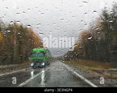 A car drives down a wet road while rain drops cover the windshield on a ...