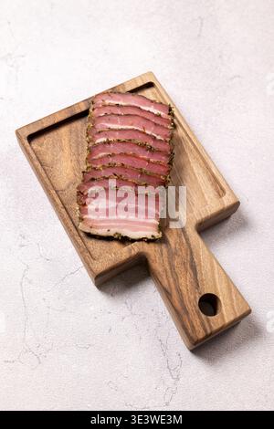 Thinly sliced smoked pork belly arranged on rustic wooden cutting board ...