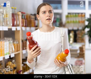 Female shopper chooses peach juice or tomato juice while shopping in ...