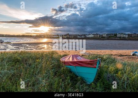The sun sets over the beach, casting light through dark clouds ...