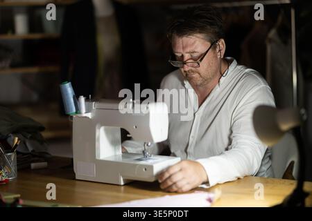 Man seamstress operating by sewing machine, manufactures clothing ...