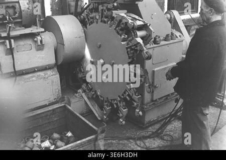 A worker operates a machine processing a rotating cylindrical metal ...