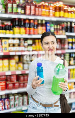 Female customer choosing soft drinks in grocery store, looking at ...