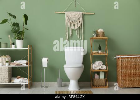 Toilet bowl, shelving units and laundry basket near beige wall in ...