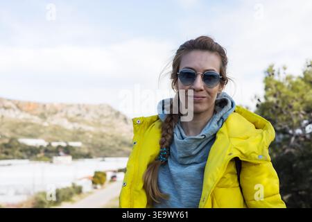 A woman wearing a yellow jacket and sunglasses stands against a ...