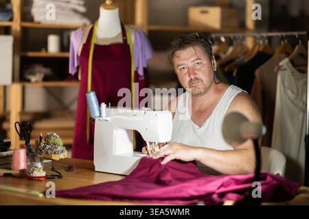 Man seamstress operating by sewing machine, manufactures clothing ...