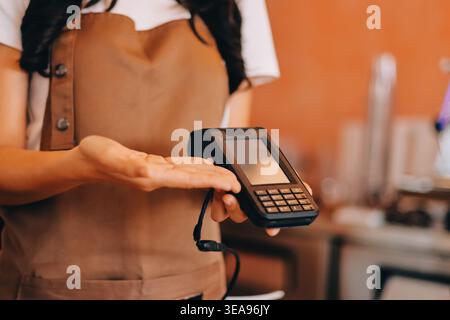 Friendly Asian female barista receives a credit card from a customer ...