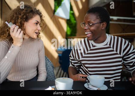 Two diverse women enjoying coffee in a cafe, looking at a digital ...