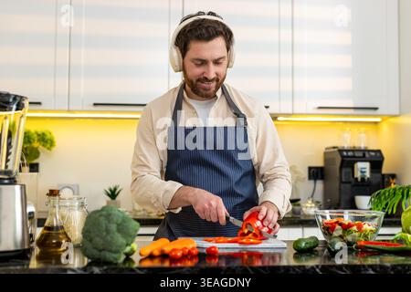Middle-aged man happily chopping red pepper for fresh salad while ...