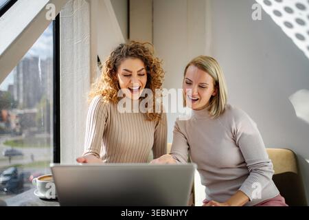 Two women sharing a laugh while collaborating on a laptop in a bright ...