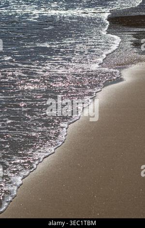 Gentle sea waves washing sandy beach near rocky coastline under clear ...