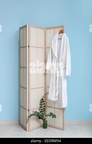 White bathrobe hanging on folding screen against yellow background ...