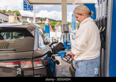 Woman refueling black automobile at gas station with blue fuel pump ...