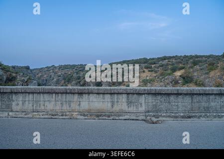 Ancient stone bridge overlooks tranquil pond. Red flowers bloom along ...