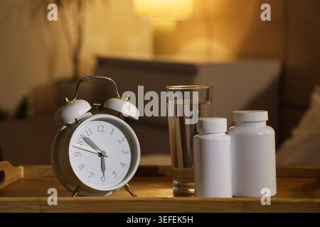 Alarm clock with pill bottles and glass of water on table in room Stock ...