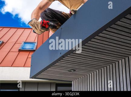 Worker use power tools to secure metal roofing panels on building under ...