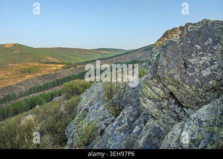 A lichen-covered rocky mountainside overlooks rolling green hills and ...