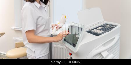 Professional cosmetologist operating a modern laser machine in a bright ...