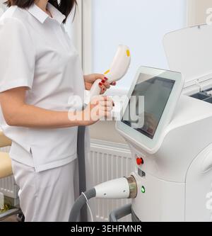 Professional cosmetologist operating a modern laser machine in a bright ...